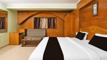 Quarto de hotel com uma cama grande, um banquinho de madeira, uma mesa pequena e um espelho.