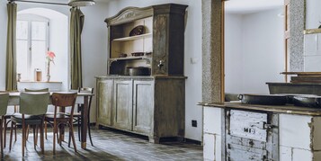 Uma cozinha com armários de madeira, uma mesa de jantar com cadeiras e uma janela com cortinas.