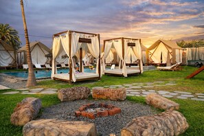 Resort com várias tendas, piscina e fogueira rodeada por pedras.