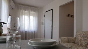 Uma área de jantar com uma mesa posta para dois, um copo de água e uma porta ao fundo.