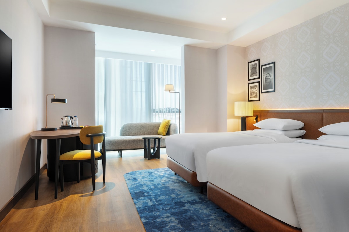 Quarto de hotel com cama, escrivaninha, poltrona, sofá e vista para o exterior.