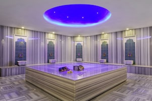 Um quarto amplo e quadrado, com uma área de estar central, várias janelas com vidro decorativo e um teto com luminária circular.