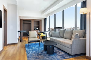 Uma sala de estar moderna com um sofá, poltronas, uma mesa de centro e vista da cidade através de grandes janelas.