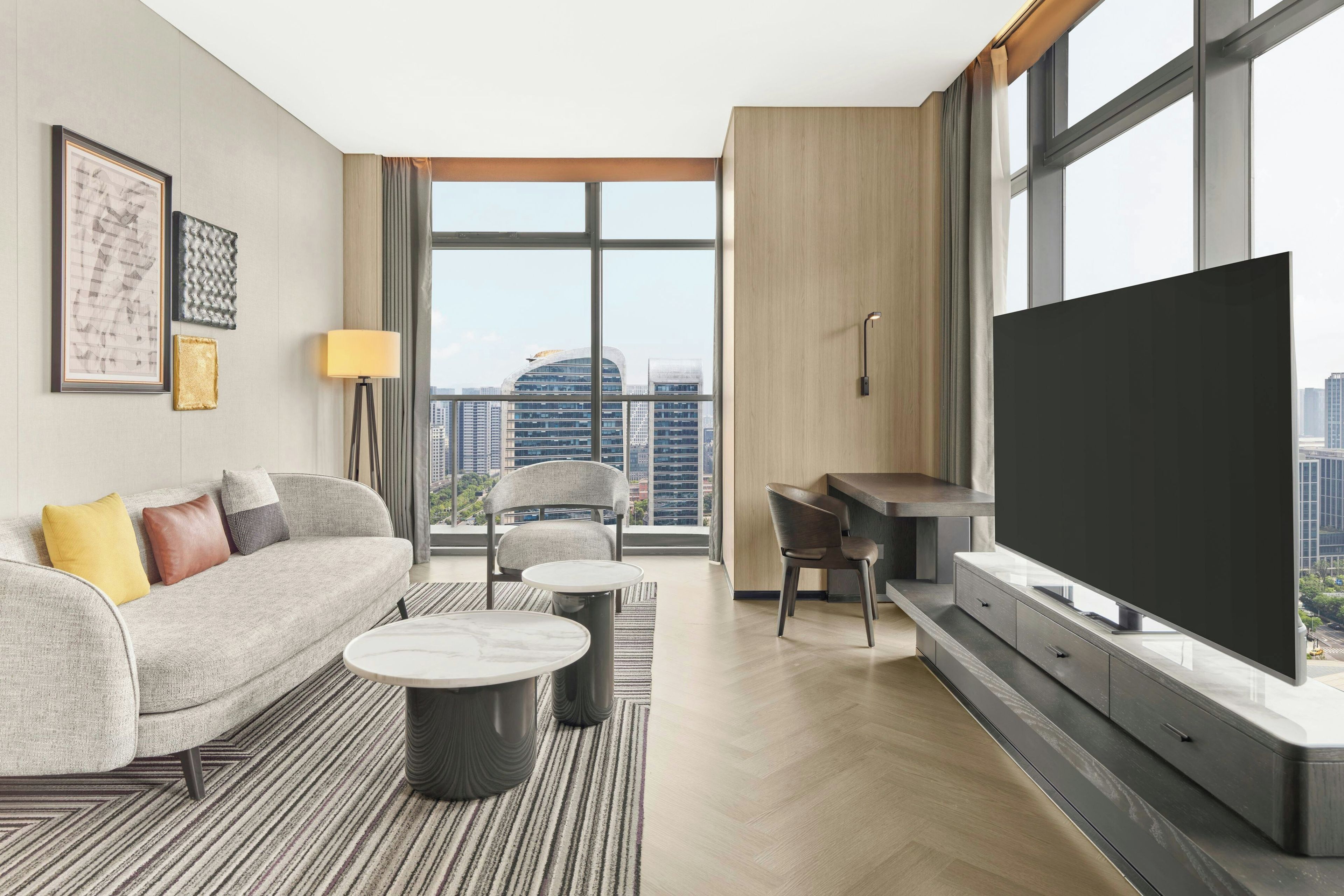 Uma sala de estar moderna com sofá, duas poltronas, mesa de centro, TV e vista para a cidade.