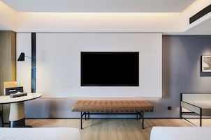Quarto moderno com uma grande TV de tela plana presa na parede, uma mesa redonda com abajur, um banco e um pequeno sofá.