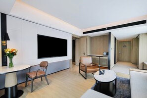 Quarto de hotel moderno com televisão de tela plana, duas poltronas de couro, uma mesa redonda pequena e uma cafeteira.