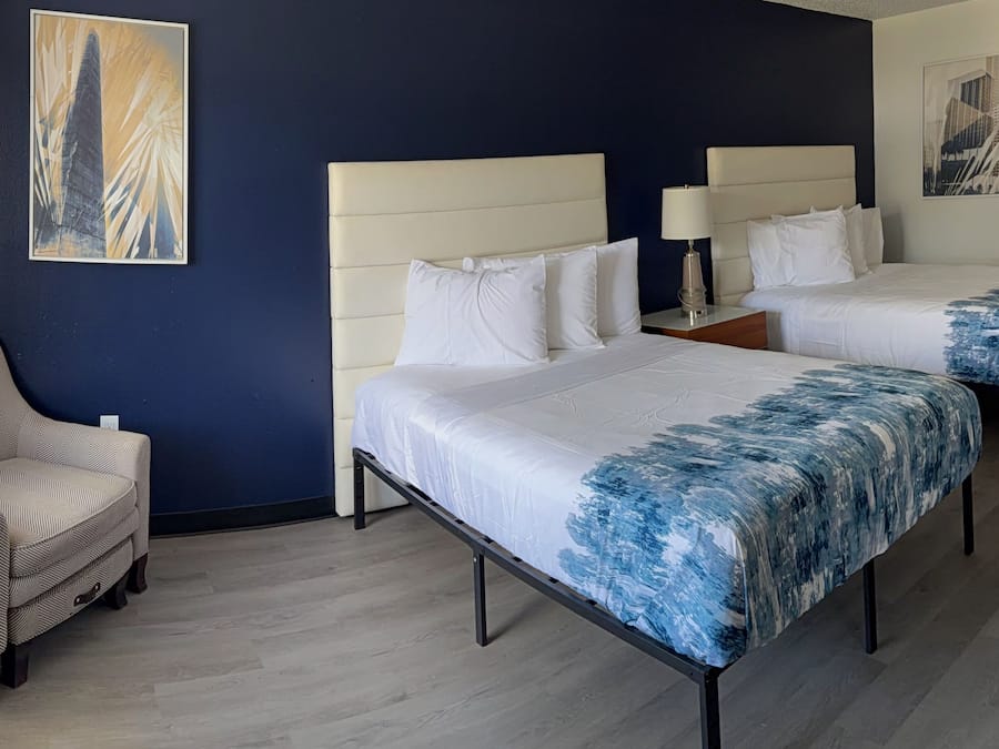 Quarto de hotel com duas camas, uma cadeira e obras de arte nas paredes.