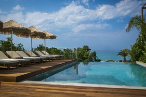 Área de piscina com espreguiçadeiras e guarda-sóis, com vista para um céu azul e o oceano.
