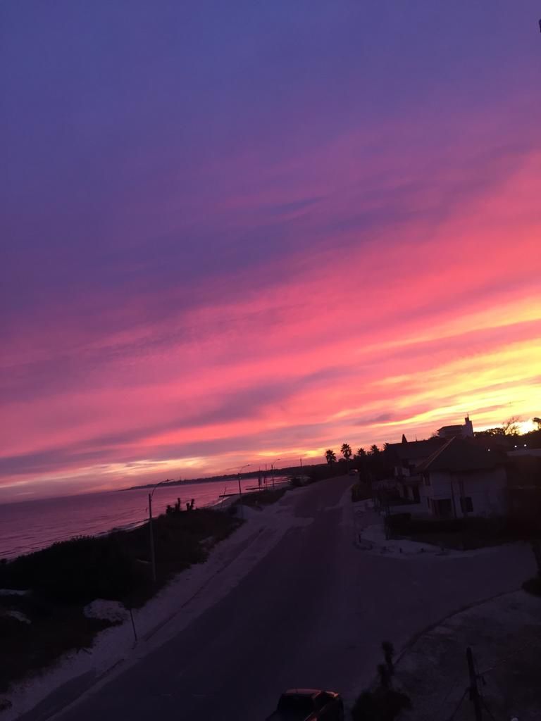Uma estrada costeira com casas à direita e um céu ao pôr do sol.