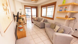 Uma sala de estar com sofá, televisão, mesa lateral de madeira e janela.