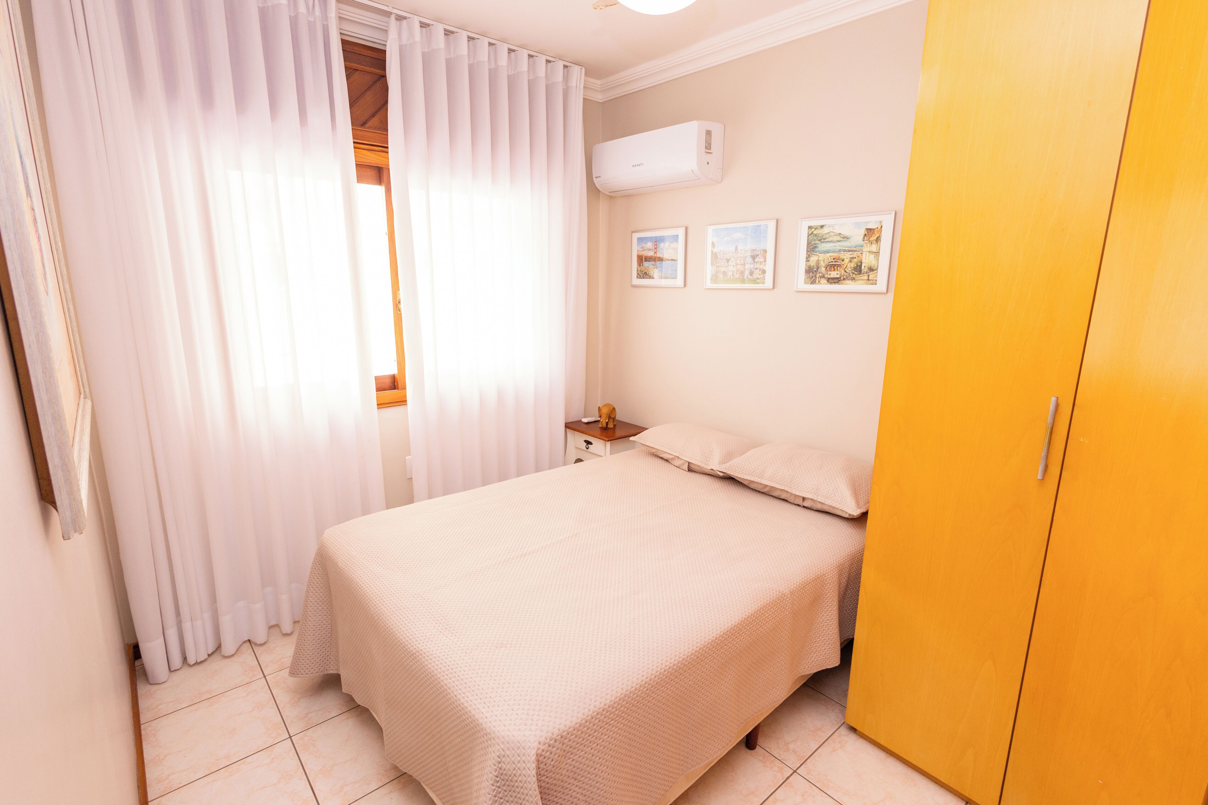 Quarto com cama, mesa de cabeceira, guarda-roupa e janela com cortinas.