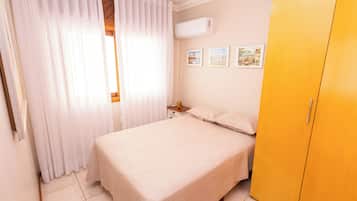 Quarto com cama, mesa de cabeceira, guarda-roupa e janela com cortinas.