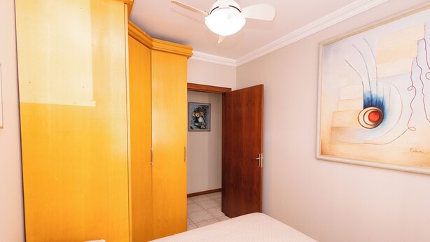 Quarto com uma cama, guarda-roupa de madeira, ventilador de teto e um quadro na parede.