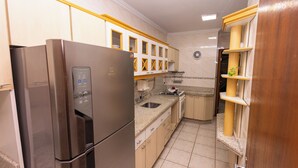 Uma cozinha compacta com geladeira de aço inoxidável, armários de madeira, uma pia e um relógio na parede.