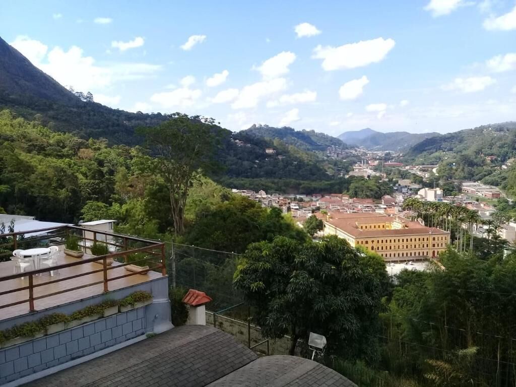 Zona residencial com vista para um vale e montanhas, um edifício com telhado vermelho e uma varanda com mobiliário de exterior.