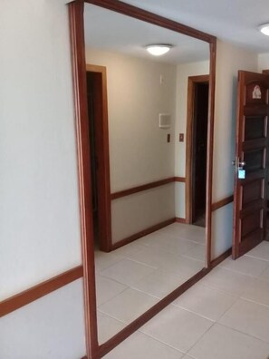 Um corredor com um espelho de madeira, soalho em azulejos e uma porta que dá para outro quarto.