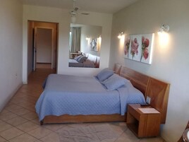 Quarto com cama, mesa de cabeceira, espelho e luminária na parede.