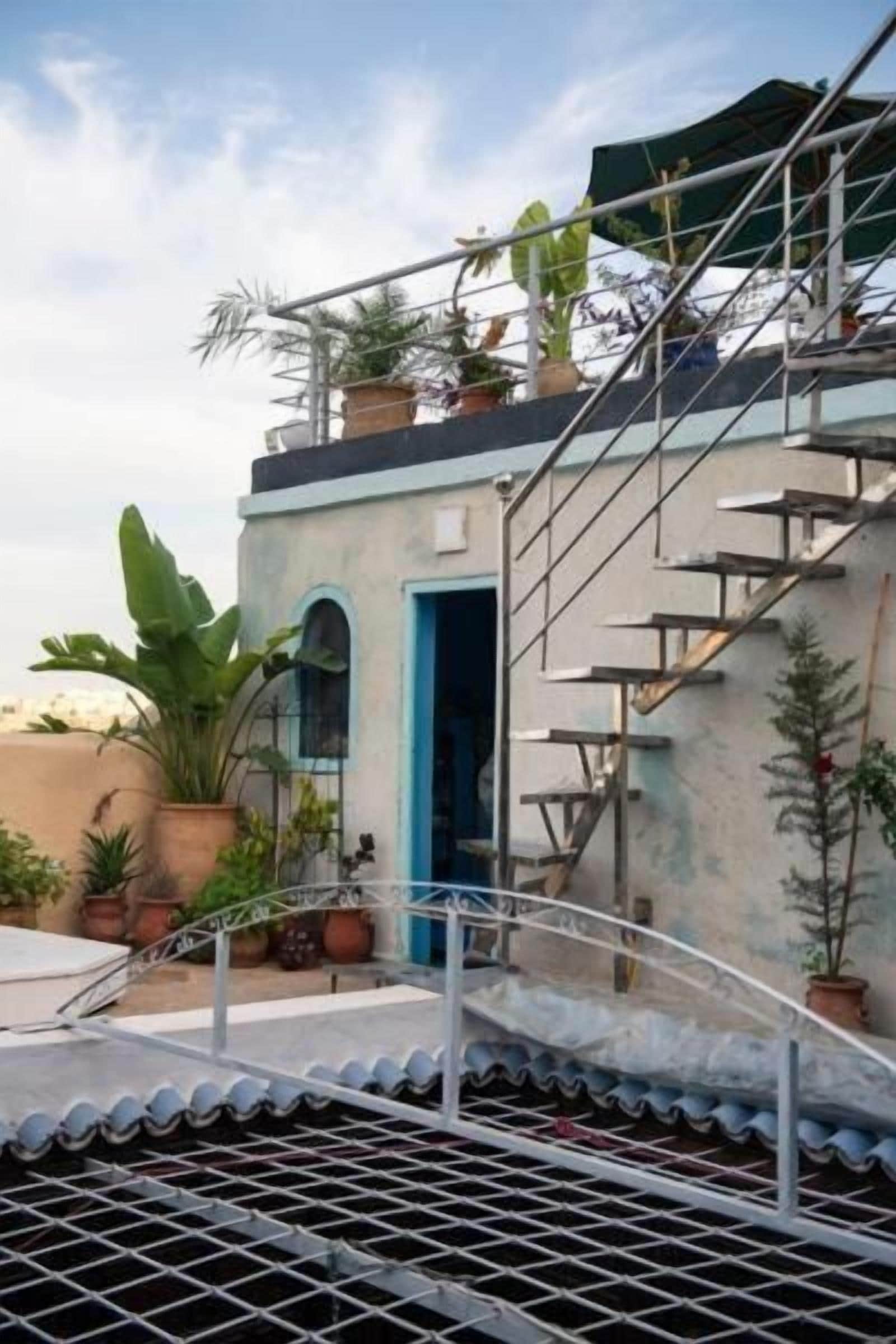 Um edifício com porta azul, escada e plantas em vasos.