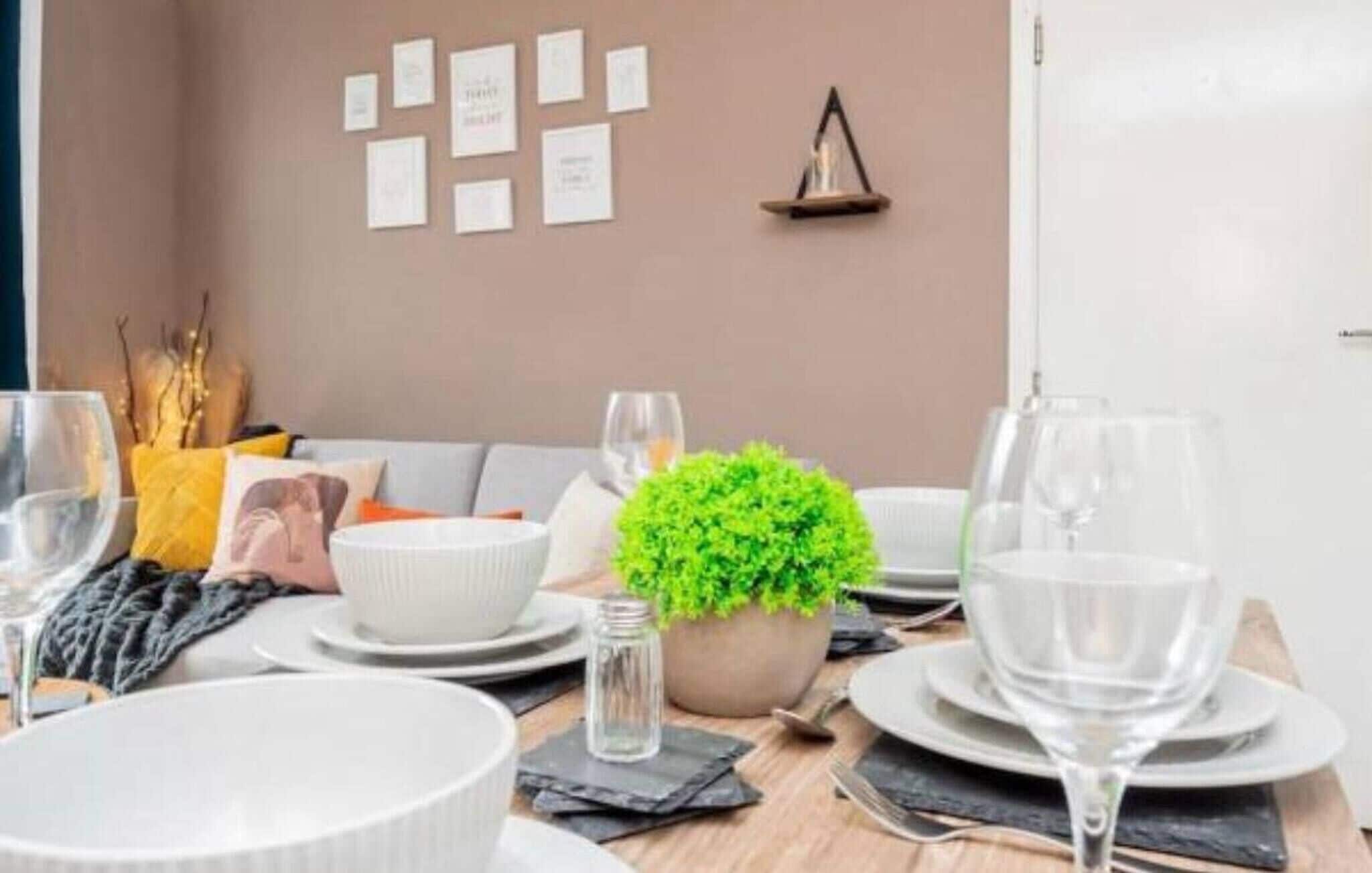 Uma mesa de jantar posta com pratos, copos e um vaso de planta.