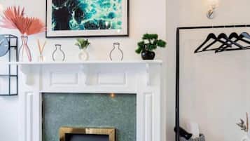Uma lareira com manto verde, um quadro abstrato emoldurado acima e um porta-casacos preto à direita.