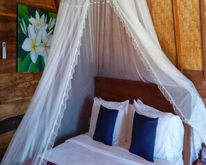 Uma cama com dossel, roupa de cama branca e duas almofadas.