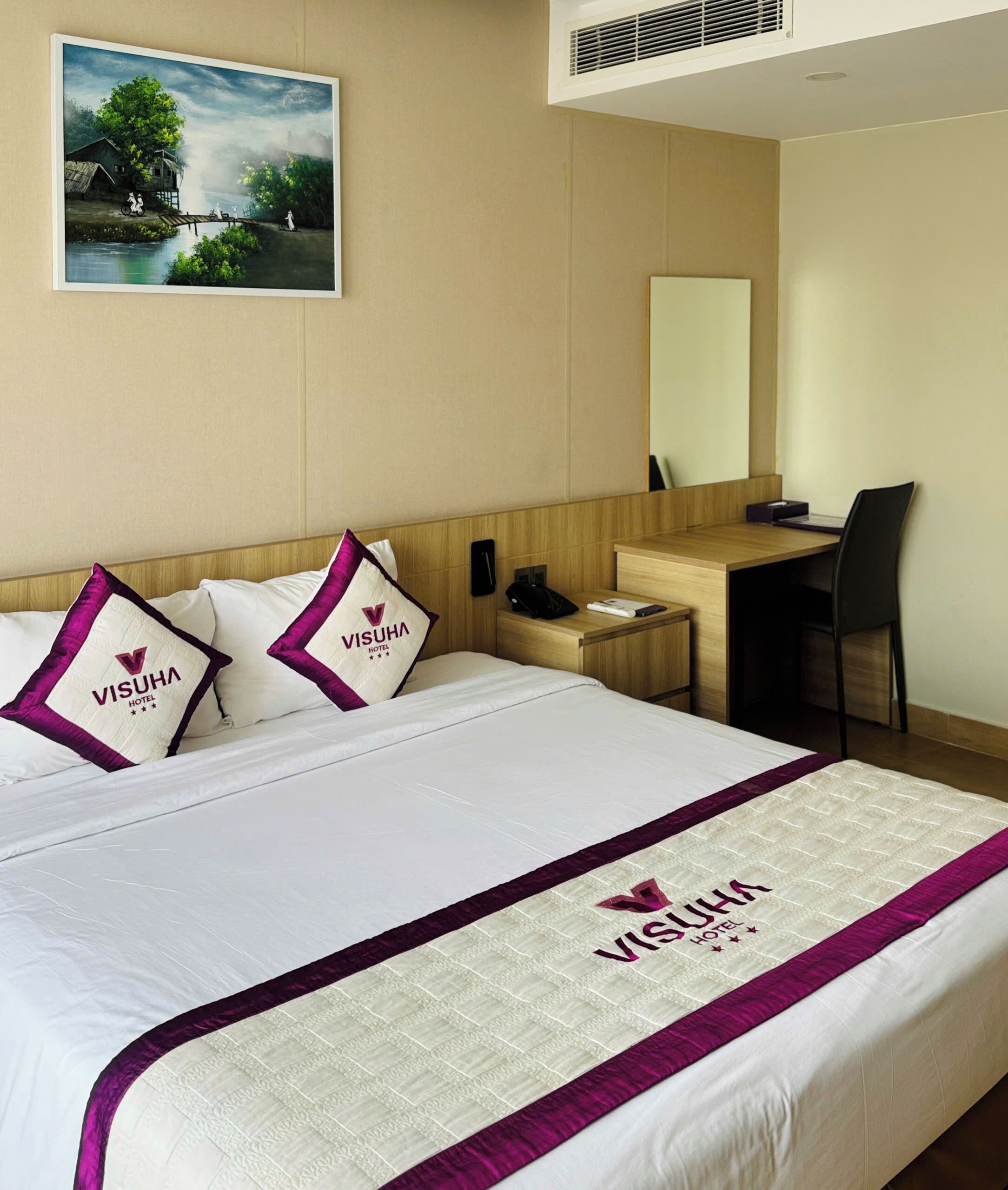 Quarto de hotel com cama, escrivaninha, cadeira, espelho e um quadro na parede.