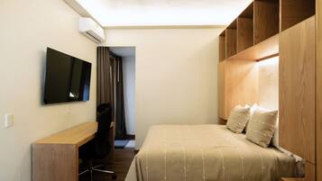 Quarto de hotel com cama, secretária, cadeira, televisão e ar condicionado.