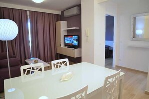 Uma sala de estar moderna com área de jantar, TV de tela plana e uma grande janela com cortinas.