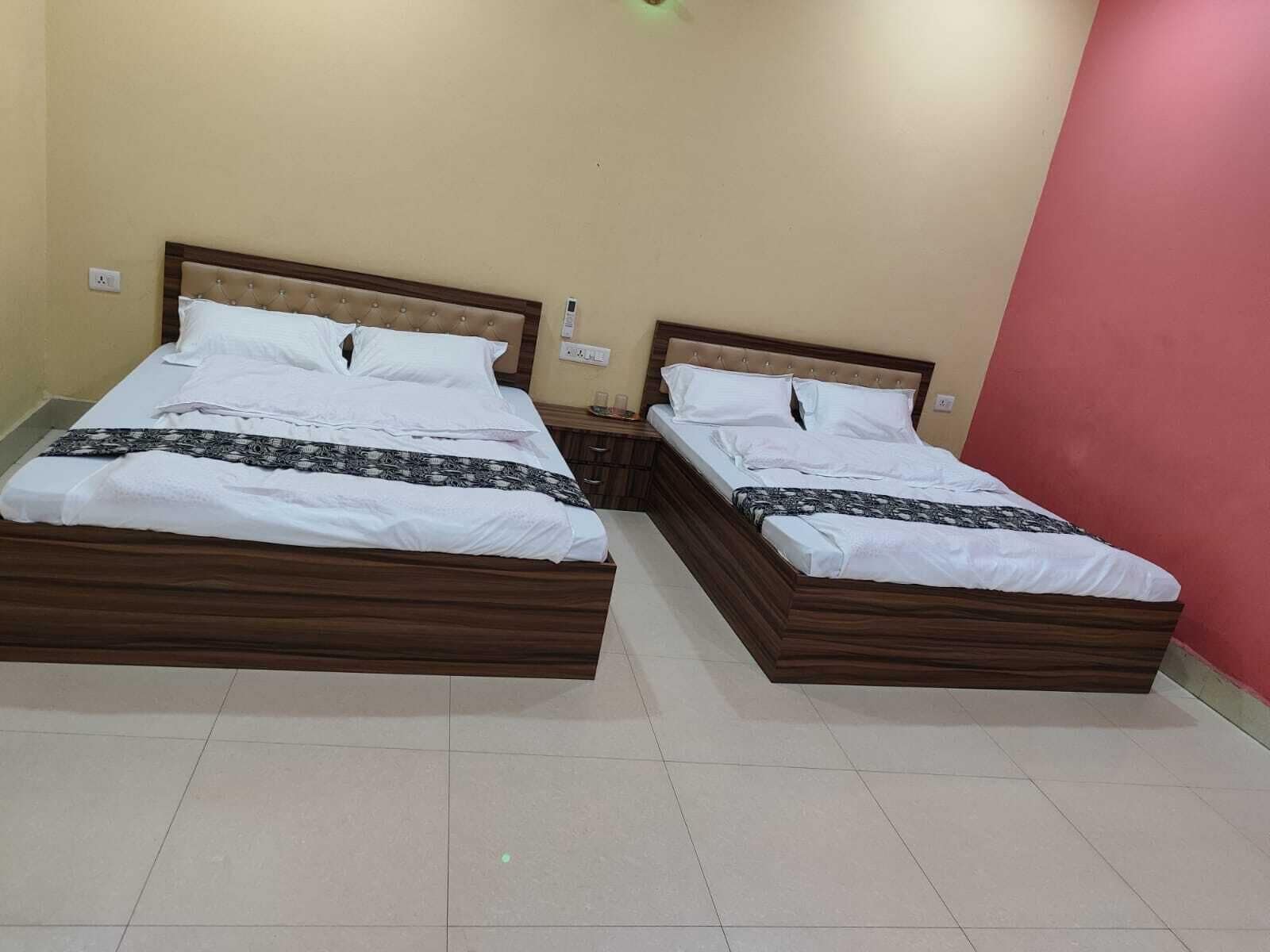 Quarto de hotel com duas camas de madeira, roupa de cama branca e uma parede de destaque vermelha.