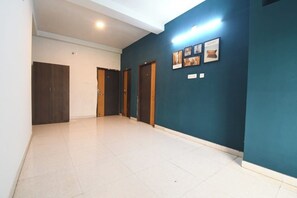 Um corredor com piso ladrilhado, parede azul escura com quadros emoldurados e uma porta de madeira.
