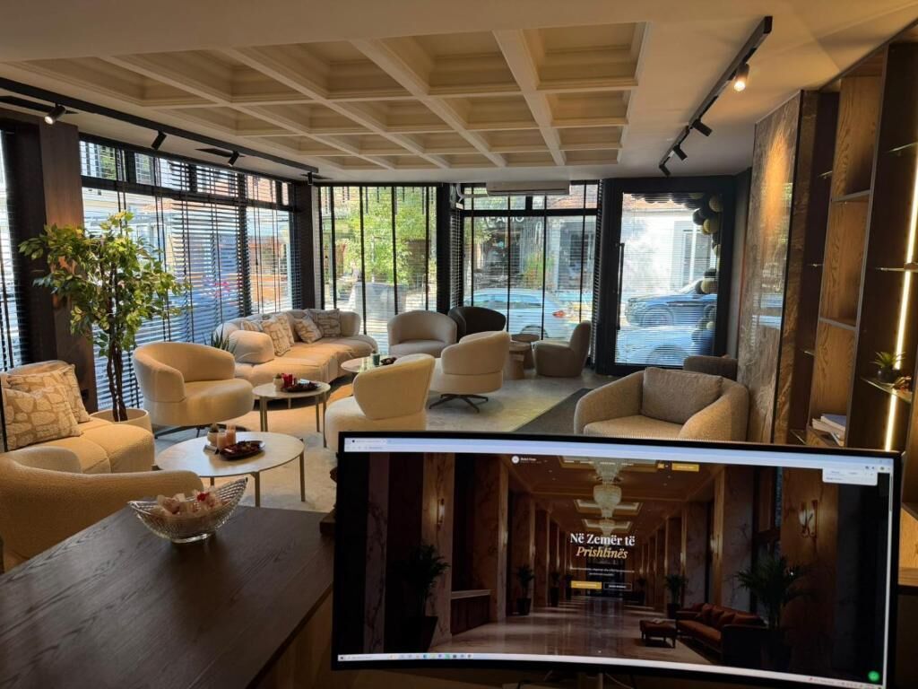 Um saguão de hotel moderno com uma grande janela, assentos confortáveis e uma tela de televisão exibindo o interior do hotel.