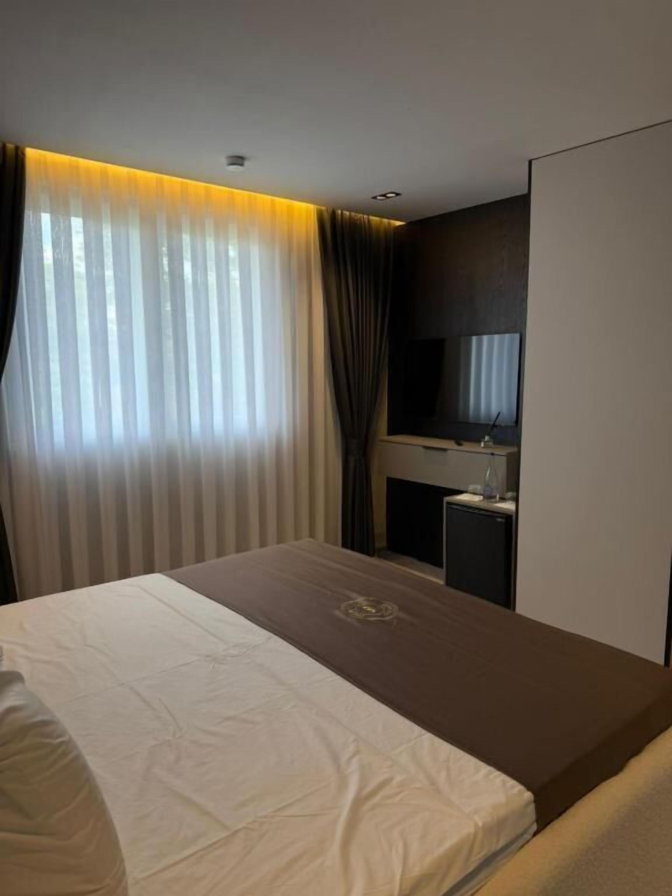 Quarto de hotel com uma cama, uma escrivaninha e uma televisão.