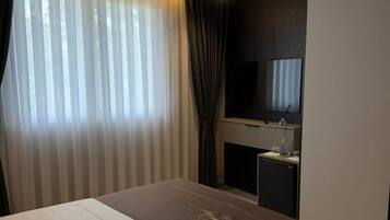 Quarto de hotel com uma cama, uma escrivaninha e uma televisão.