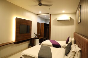 Quarto de hotel com cama, televisão, escrivaninha, guarda-roupa e ar condicionado.