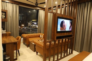 Uma sala de estar moderna com televisão, sofá de couro, mesa de centro de madeira e vista para o horizonte noturno.