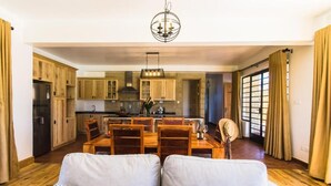 Ampla sala de estar com mesa de jantar e sofá, cozinha com armários de madeira e uma grande janela com cortinas.