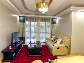 Uma sala de estar com sofá, mesa de centro, televisão e tapete vermelho.
