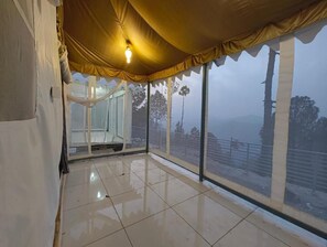 Um quarto com piso de azulejos, uma janela grande com vista para árvores e uma cerca, além de um lustre.