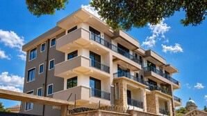 Um edifício residencial de vários andares com fachada de pedra, várias varandas e céu claro.