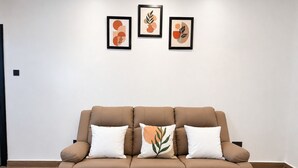 Um sofá marrom com almofadas brancas em um quarto com piso de madeira e parede branca.