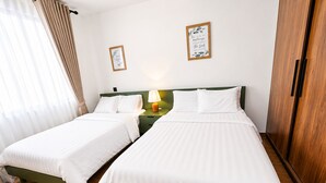 Quarto de hotel com duas camas de solteiro, uma mesa de cabeceira com luminária e um guarda-roupa.