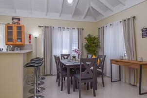 Uma área de refeições com mesa, cadeiras, balcão e cozinha equipada, com armários e extintor de incêndio.