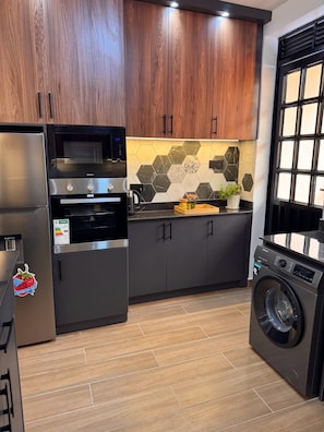 Uma cozinha moderna com geladeira de aço inoxidável, forno embutido, micro-ondas, máquina de lavar e armários de madeira.