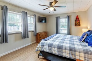 Um quarto com cama, cômoda, ventilador de teto e televisão na parede.