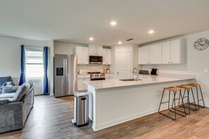 Uma cozinha moderna com armários brancos, eletrodomésticos de aço inoxidável e uma ilha central com banquetas.