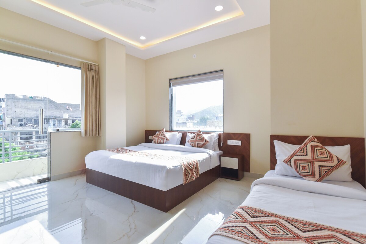 Quarto de hotel com uma cama grande, uma cama menor, janela com vista para a cidade e varanda.