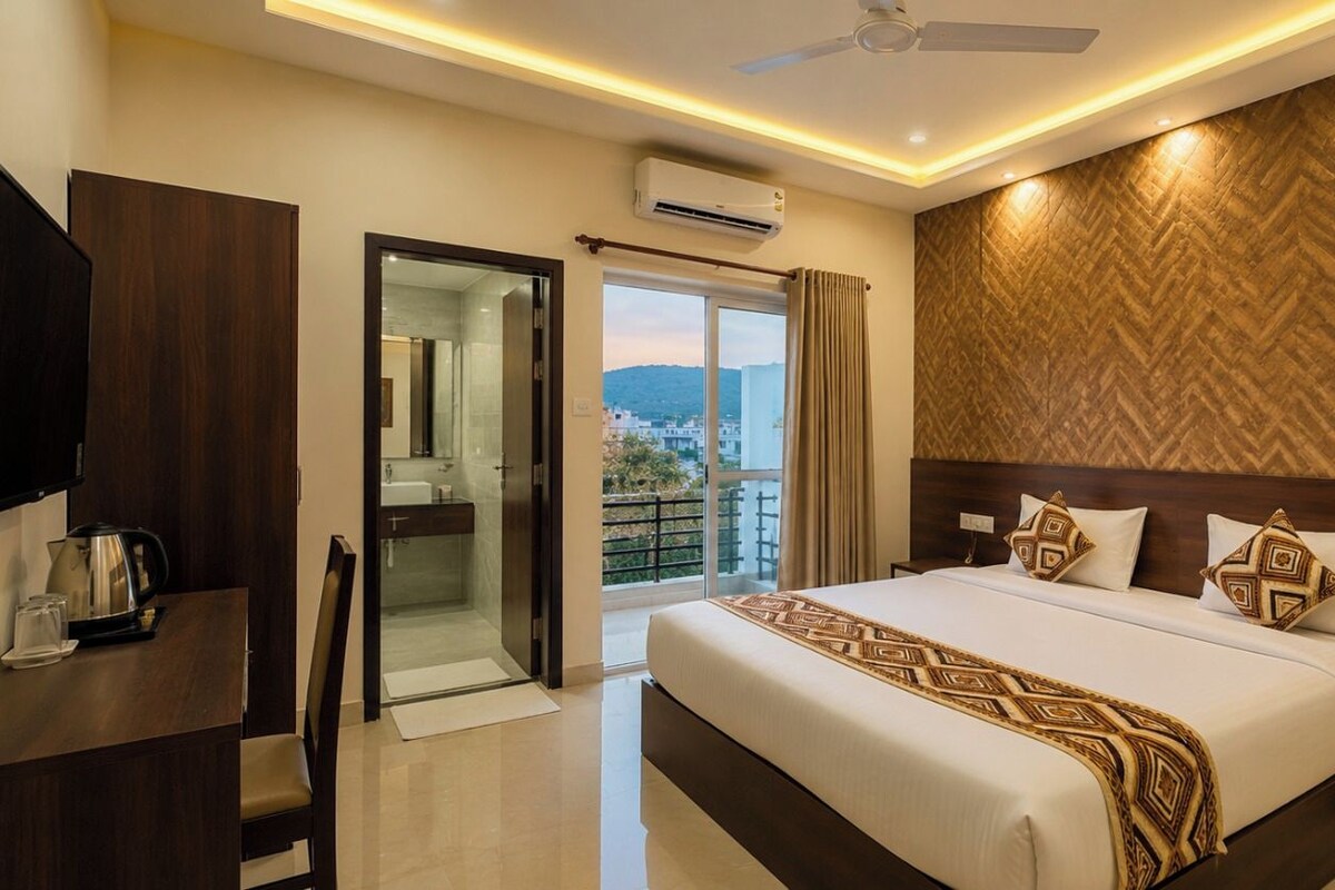 Quarto de hotel com cama, mesa de cabeceira e vista para o exterior.