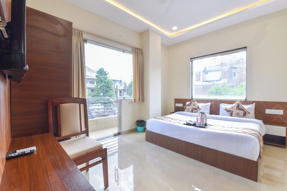 Quarto de hotel com cama, televisão, cadeira e janela com vista para edifícios.