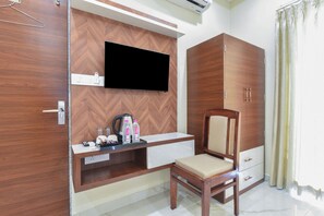 Quarto de hotel com guarda-roupa de madeira, televisão na parede, secretária com cadeira e uma cama.