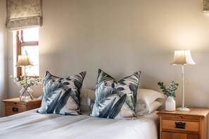 Quarto com cama, duas mesas de cabeceira, abajur e janela com cortinas.